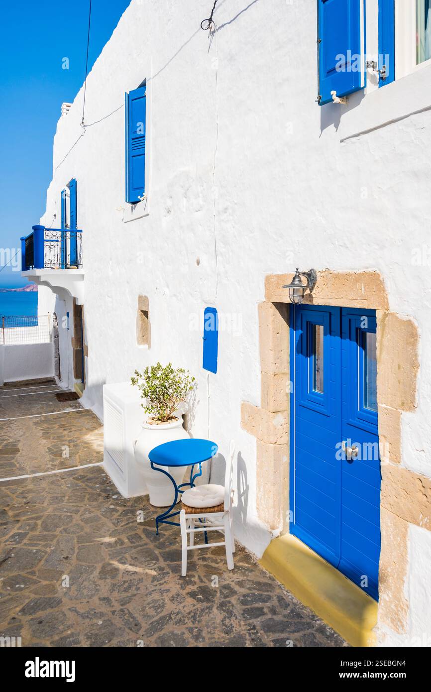 Typical white Greek house with blue door and small table with chair on ...