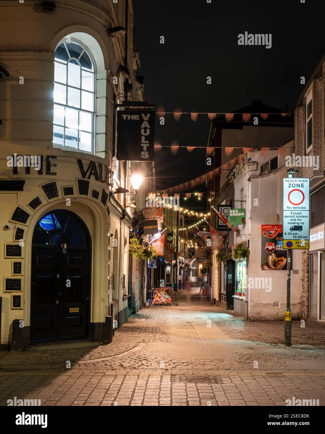The narrow traditional shop-lined Gandy Street is lit at night in ...