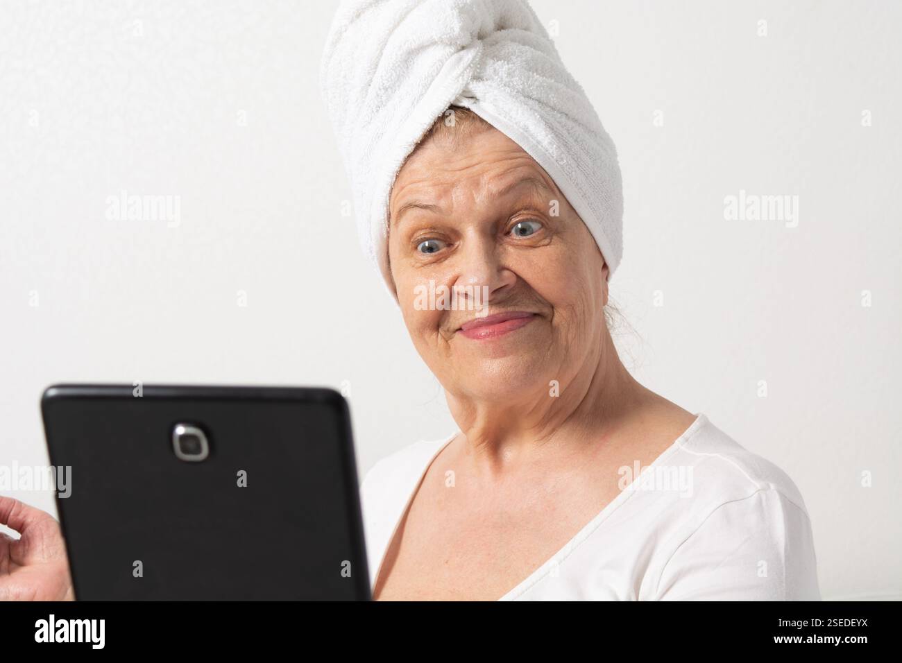 Caucasian senior woman with wrinkles talking with somebody by tablet ...