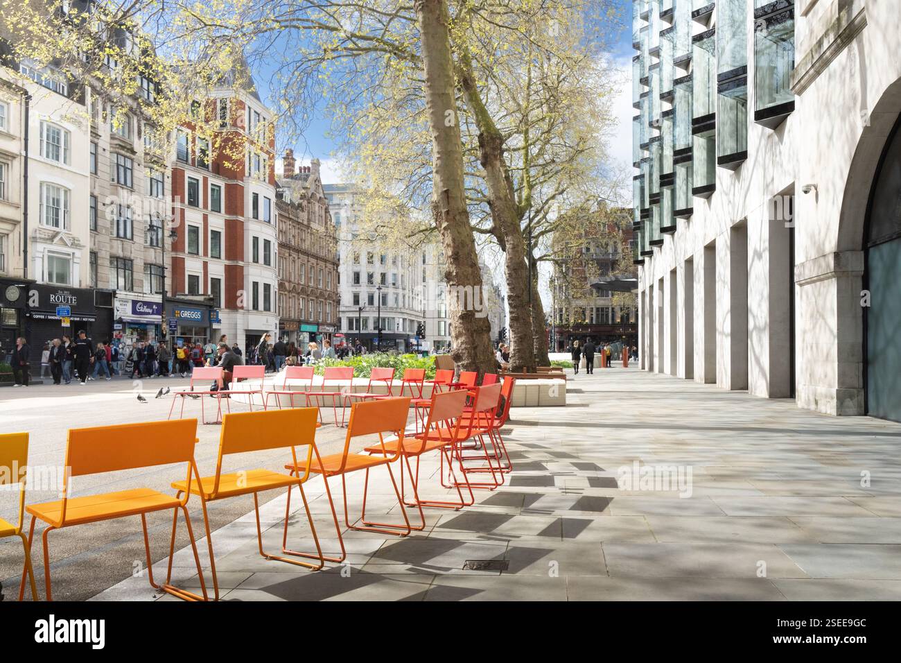 Pedestrians stroll Strand Aldwych, London, past colorful chairs in a ...