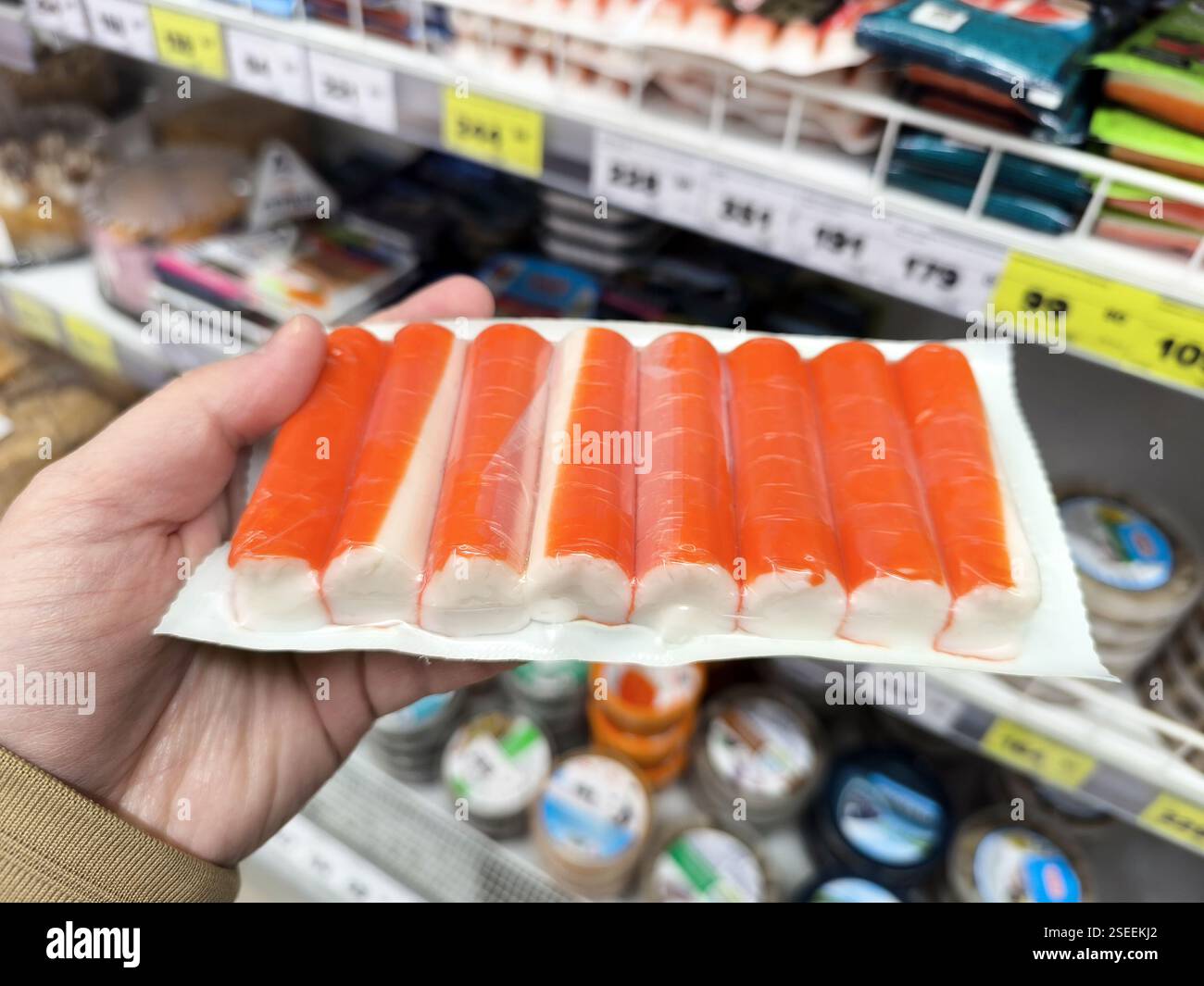 Caucasian hand holding packaged imitation crab sticks in grocery store ...