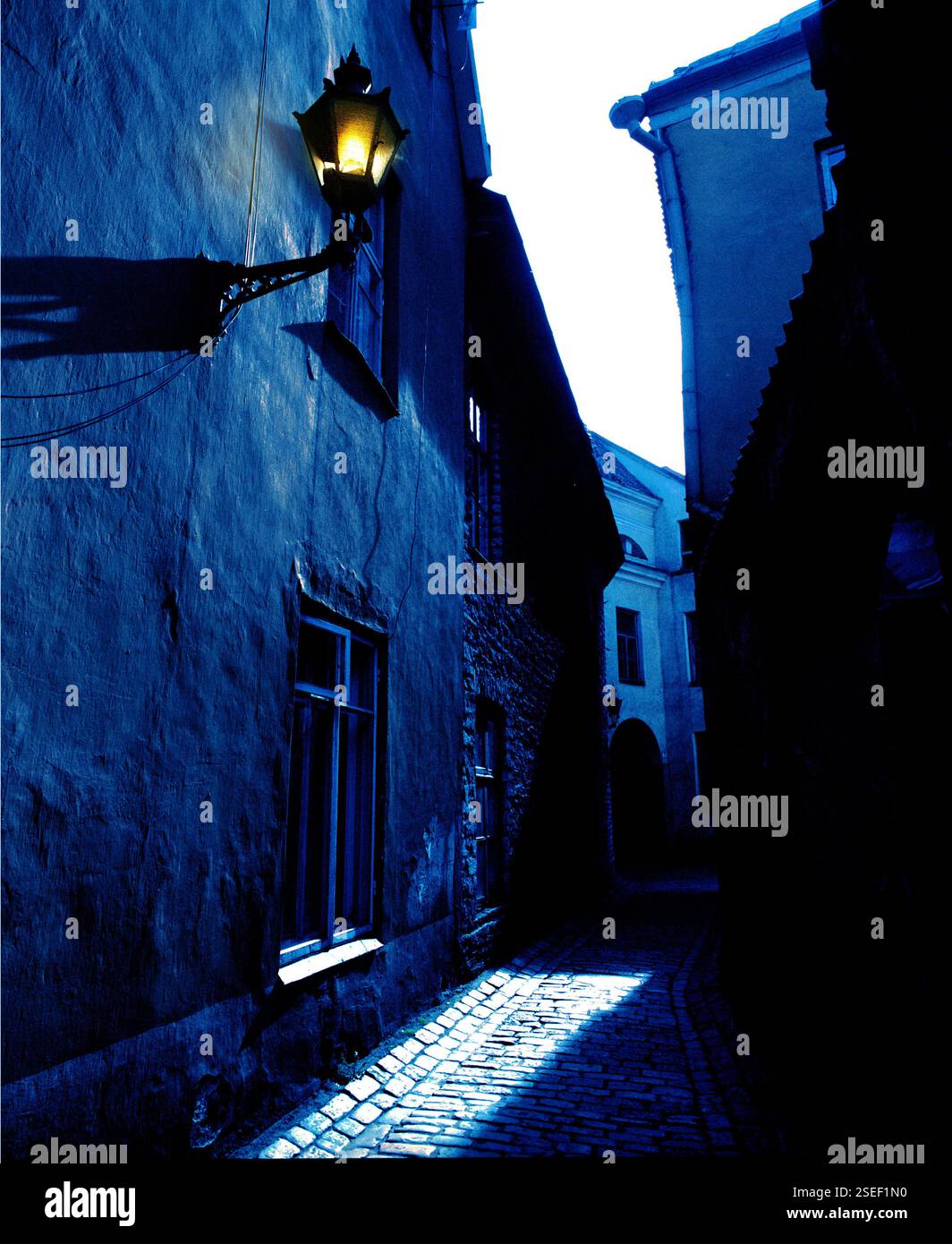 A blue alleyway with a lamp post and a shadow on the wall. The light ...