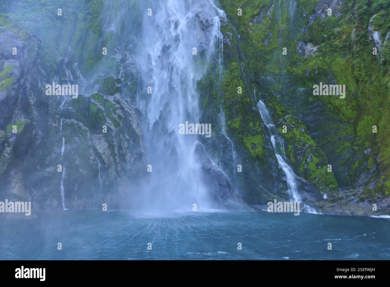 Waterfall pours over overgrown cliffs into the blue water, summer ...