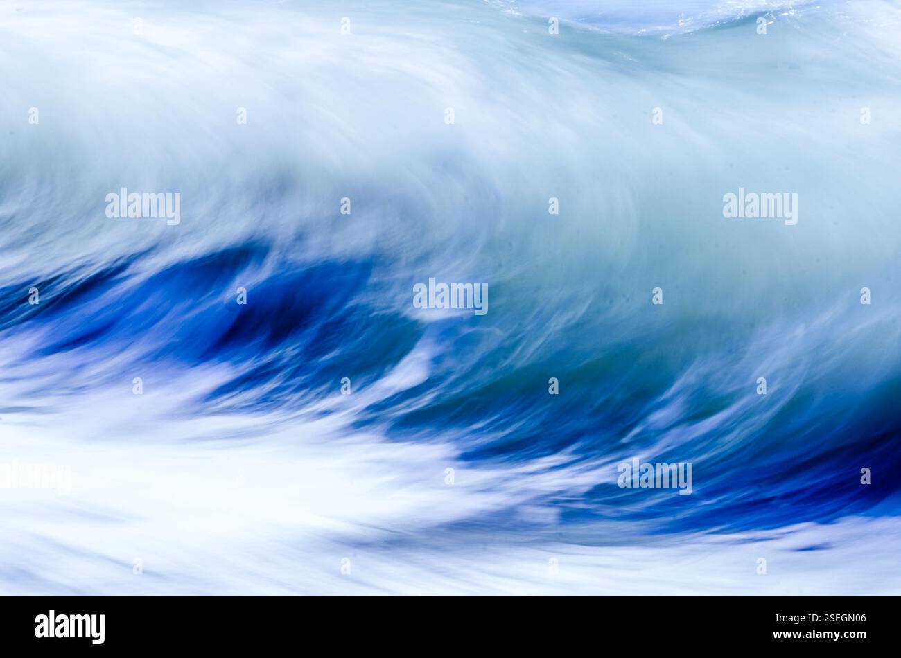A slow shutter speed captures the motion of an ocean wave in deep blue ...