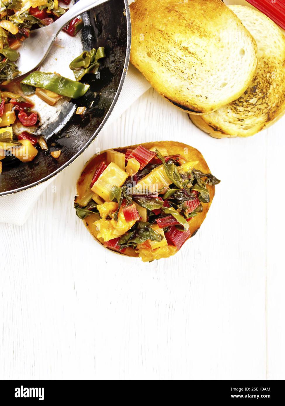 Toasted slice of bread with stewed chard, onion and orange on a wooden ...