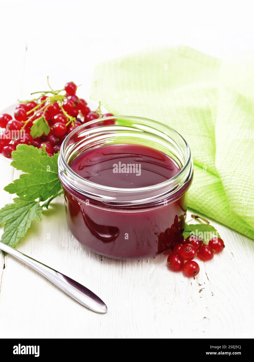 Red currant jam in a glass jar, bunches of berries with leaves, a ...