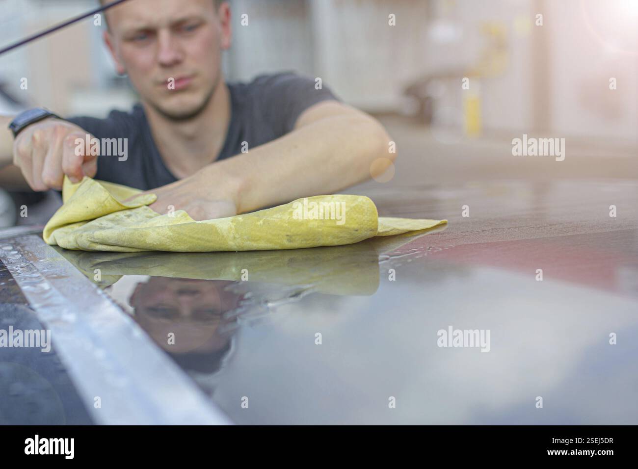 A man cleans a reflective car surface with a cloth, depicting a focused ...