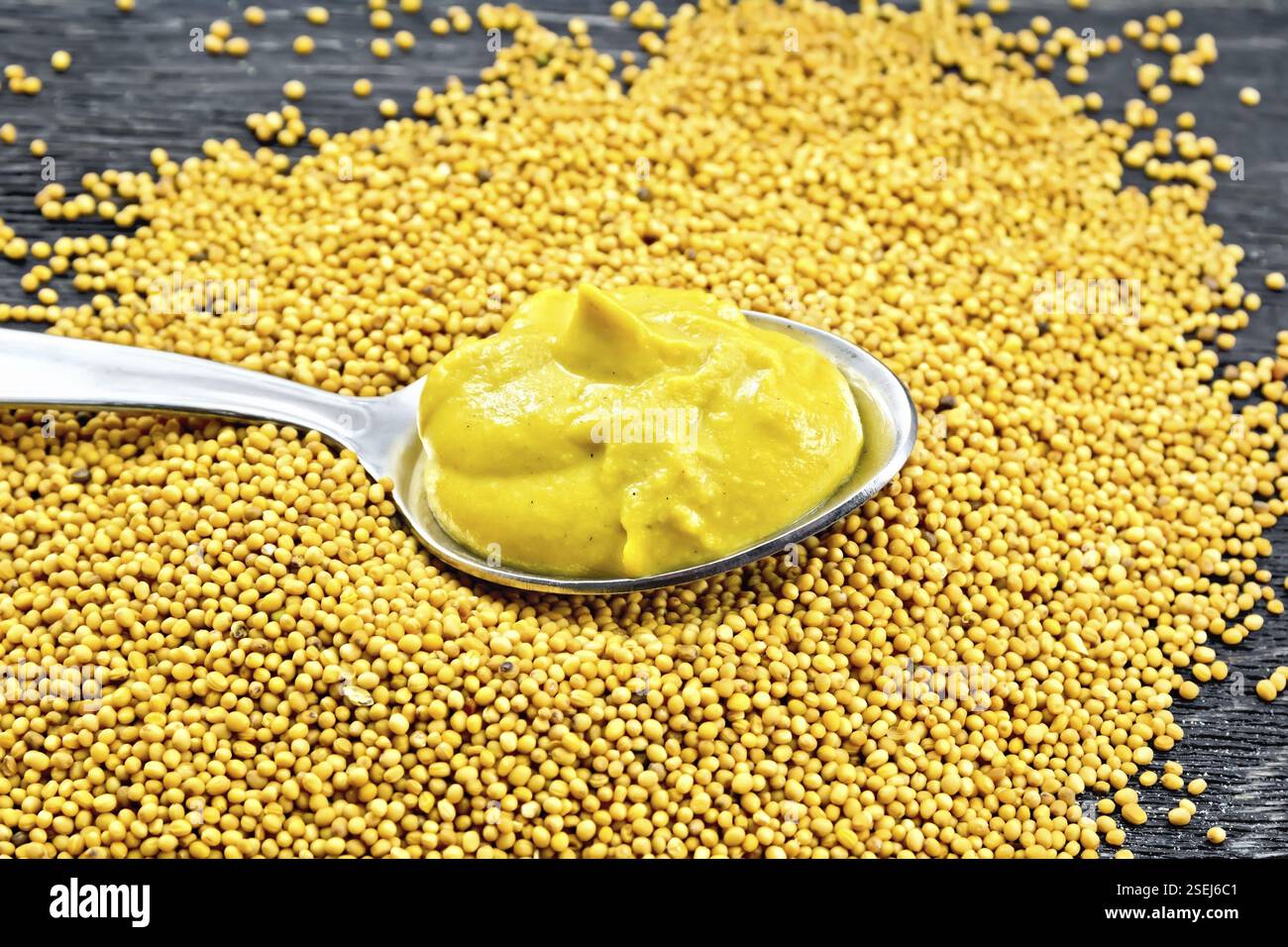 Mustard sauce in a metal spoon on mustard seeds against the background ...