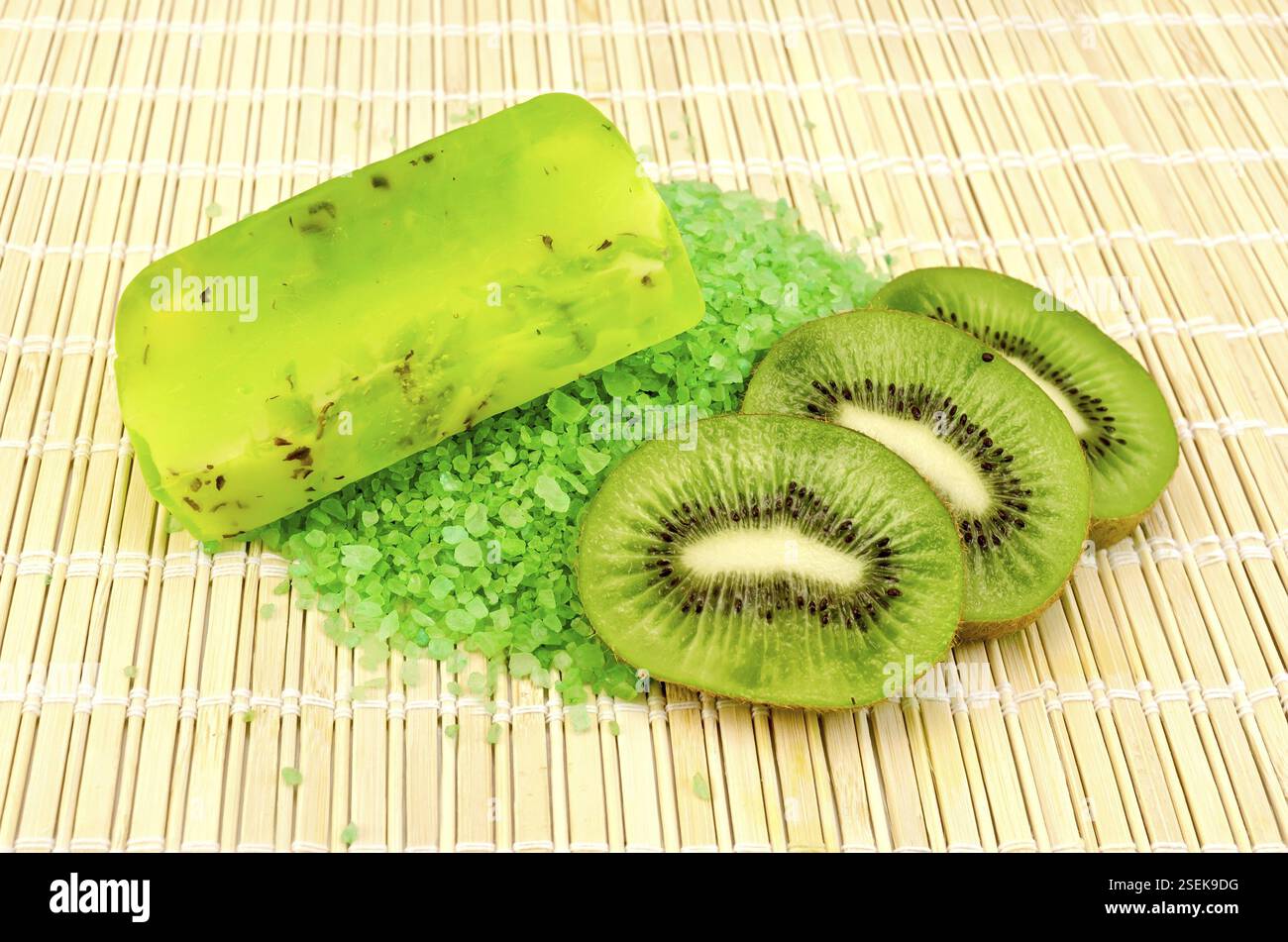 Green homemade soft soap and salt, three kiwi slices on a bamboo napkin ...