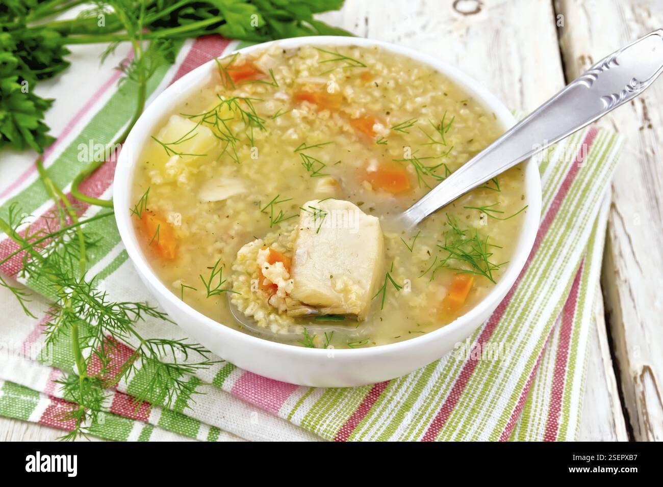Soup fish kulesh with millet, potatoes, carrots and spoon in a white ...