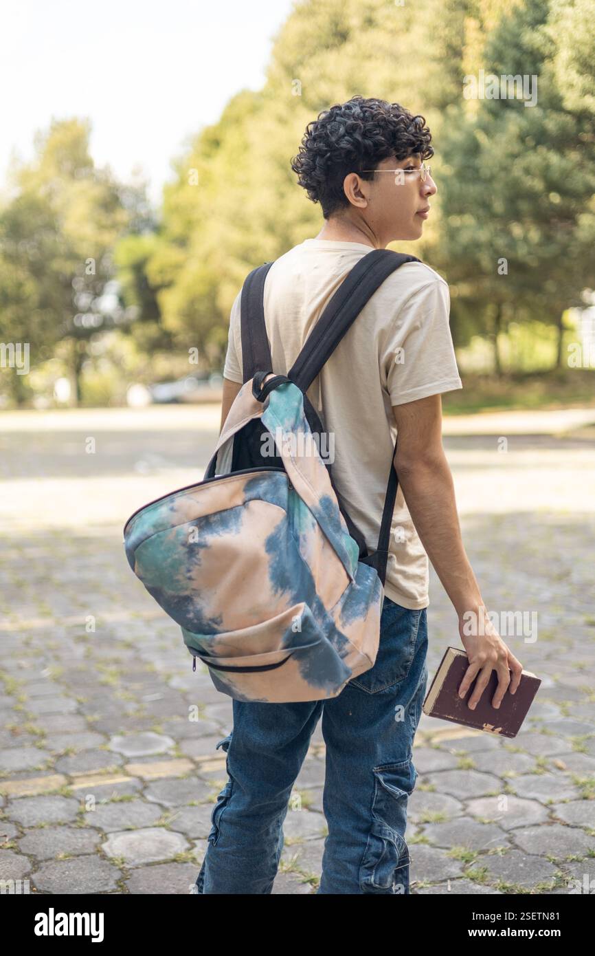 A young boy seen from behind, holding a book with a semi-open backpack on his back. Perfect for ...