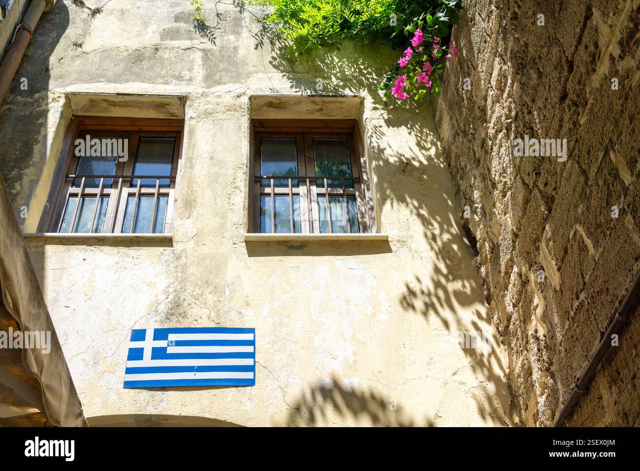 Greek flag sign attached to old wall below two barred windows and stone ...