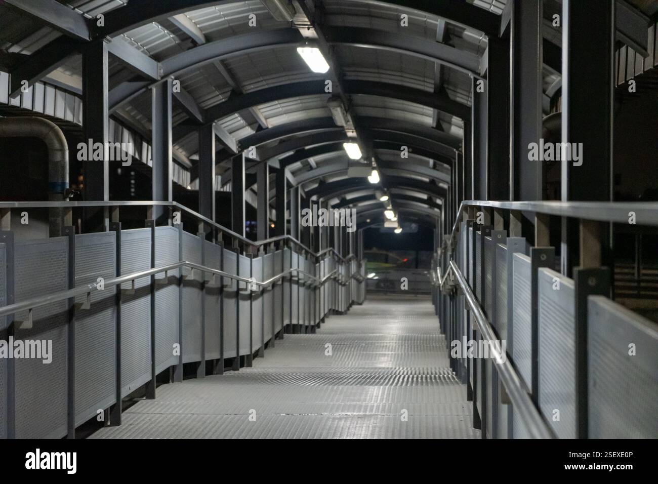 Pedestrian bridge with a metallic walkway and arched overhead structure ...
