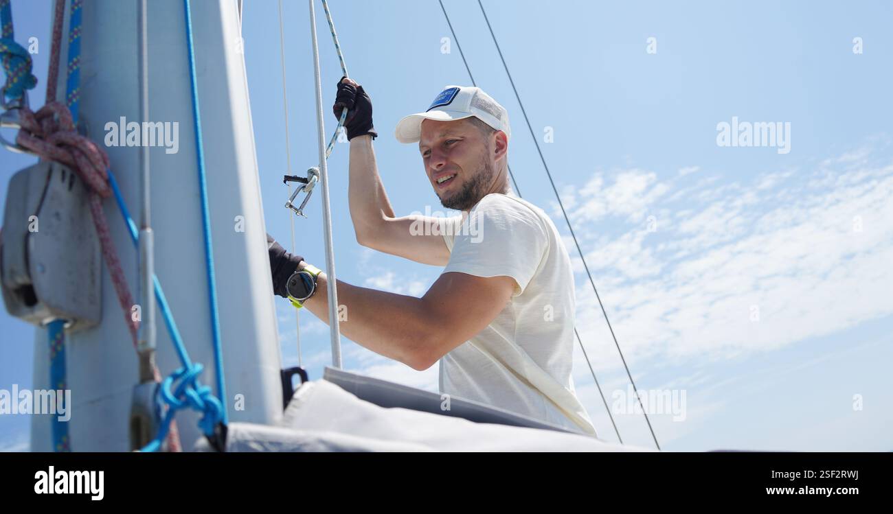 Male captain on deck of sailboat opening sails pulling the rope Stock ...