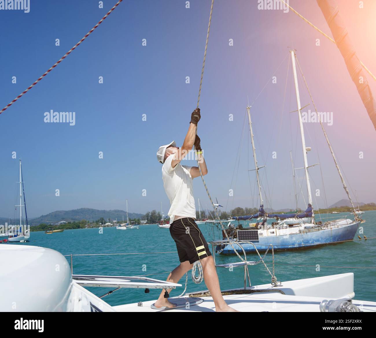 Male captain on deck of sailboat opening sails pulling the rope Stock ...