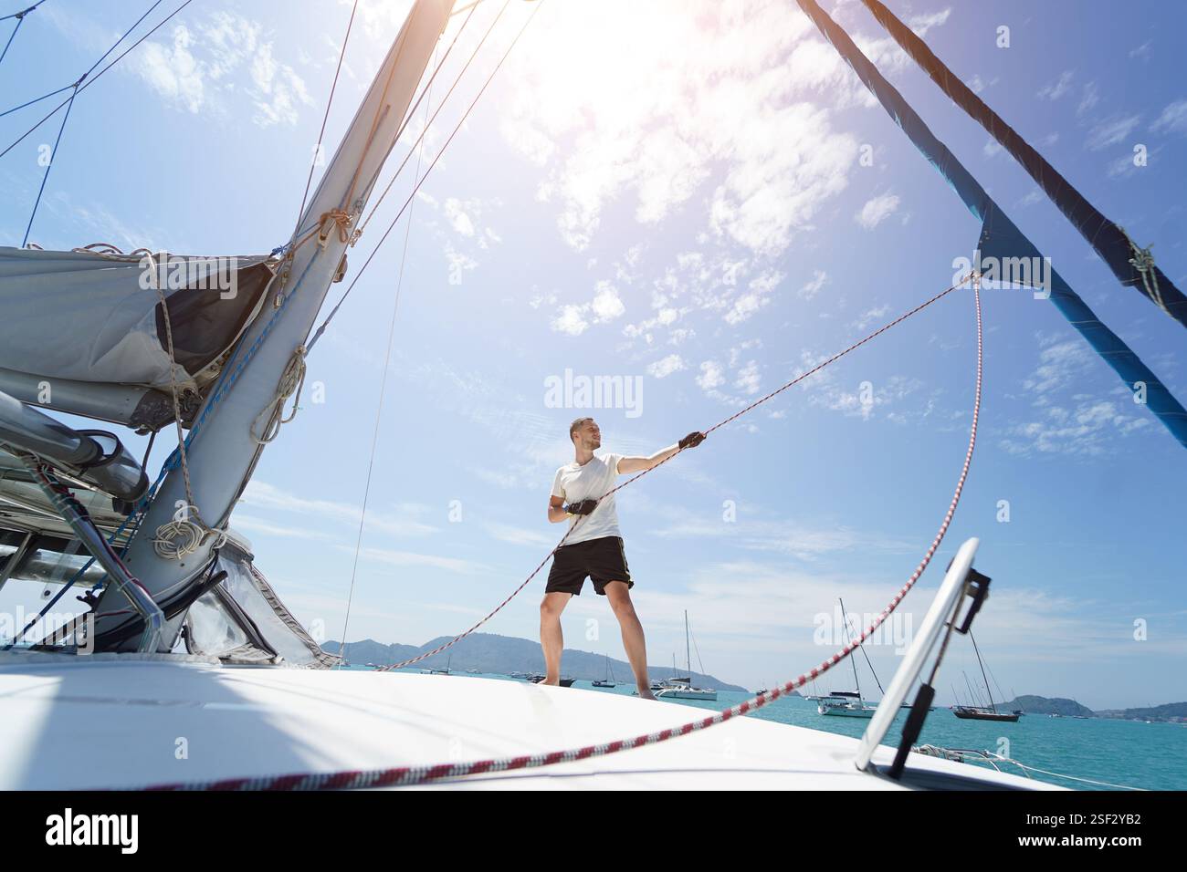 Male captain on deck of sailboat opening sails pulling the rope Stock ...
