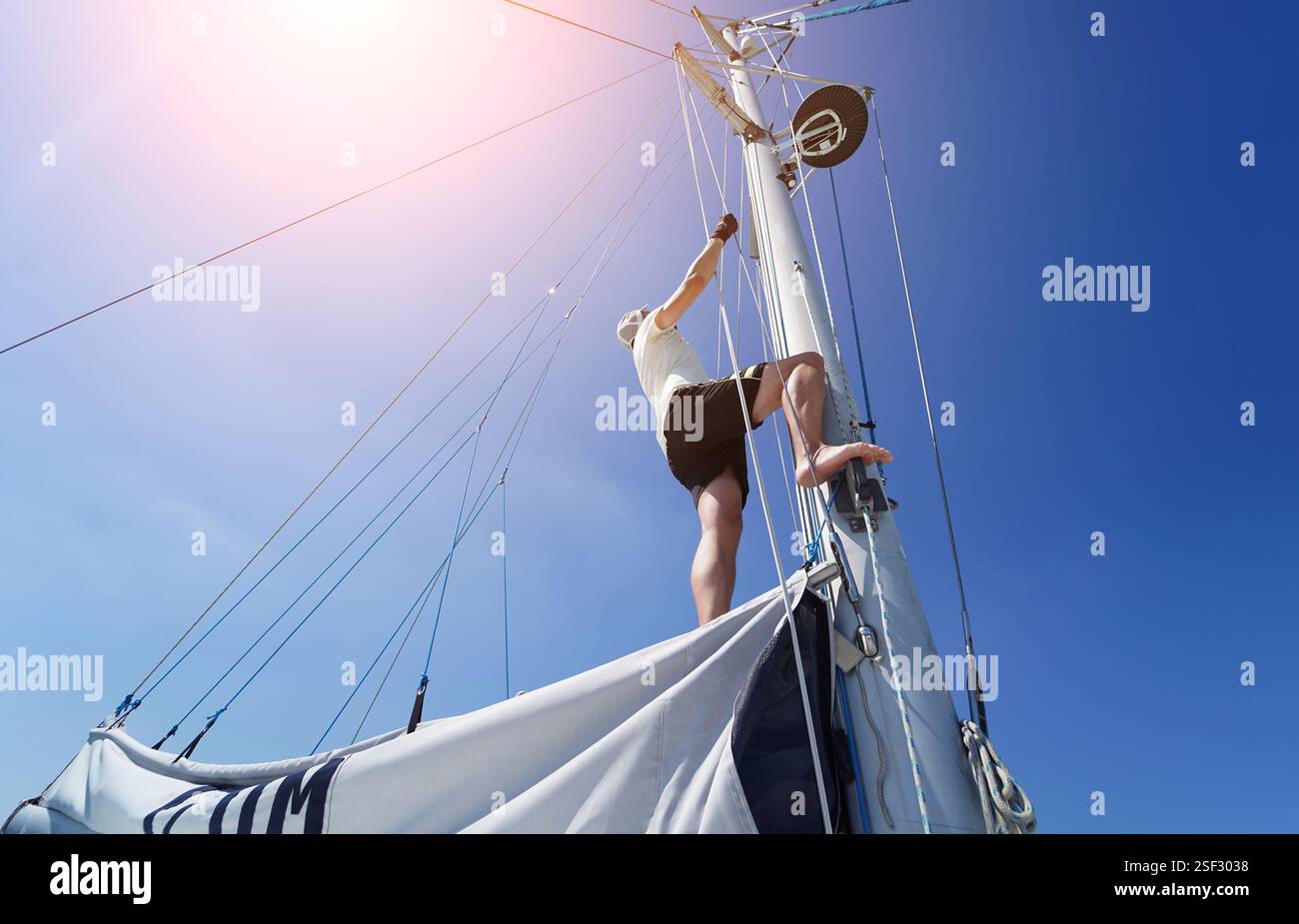 Male captain climbing mast of sailboat to check sails Stock Photo - Alamy