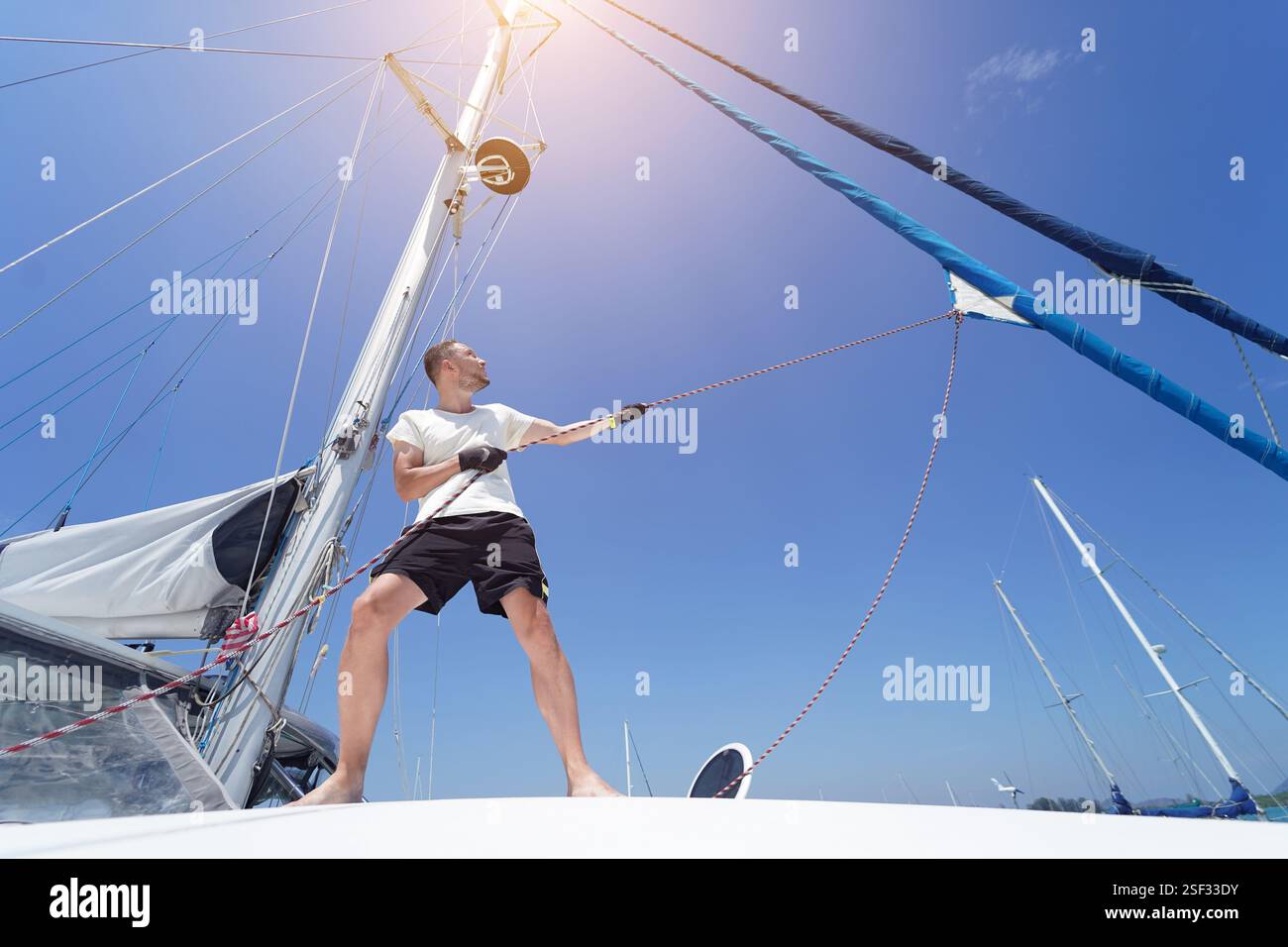 Male captain on deck of sailboat opening sails pulling the rope Stock ...