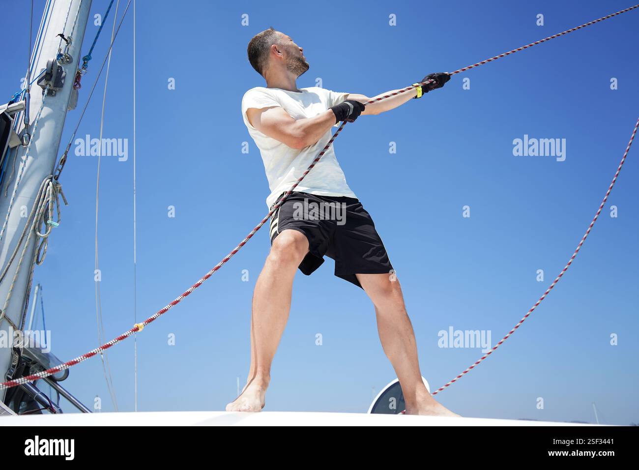 Male captain on deck of sailboat opening sails pulling the rope Stock ...