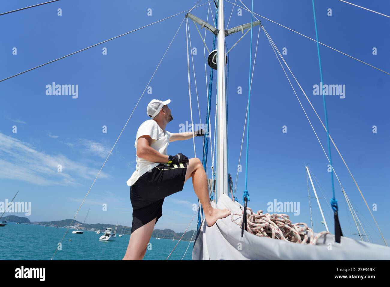 Male captain climbing mast of sailboat to check sails Stock Photo - Alamy