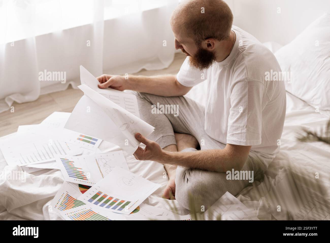 Accounting bookkeeping concept. Busy bearded man works at home on bed ...