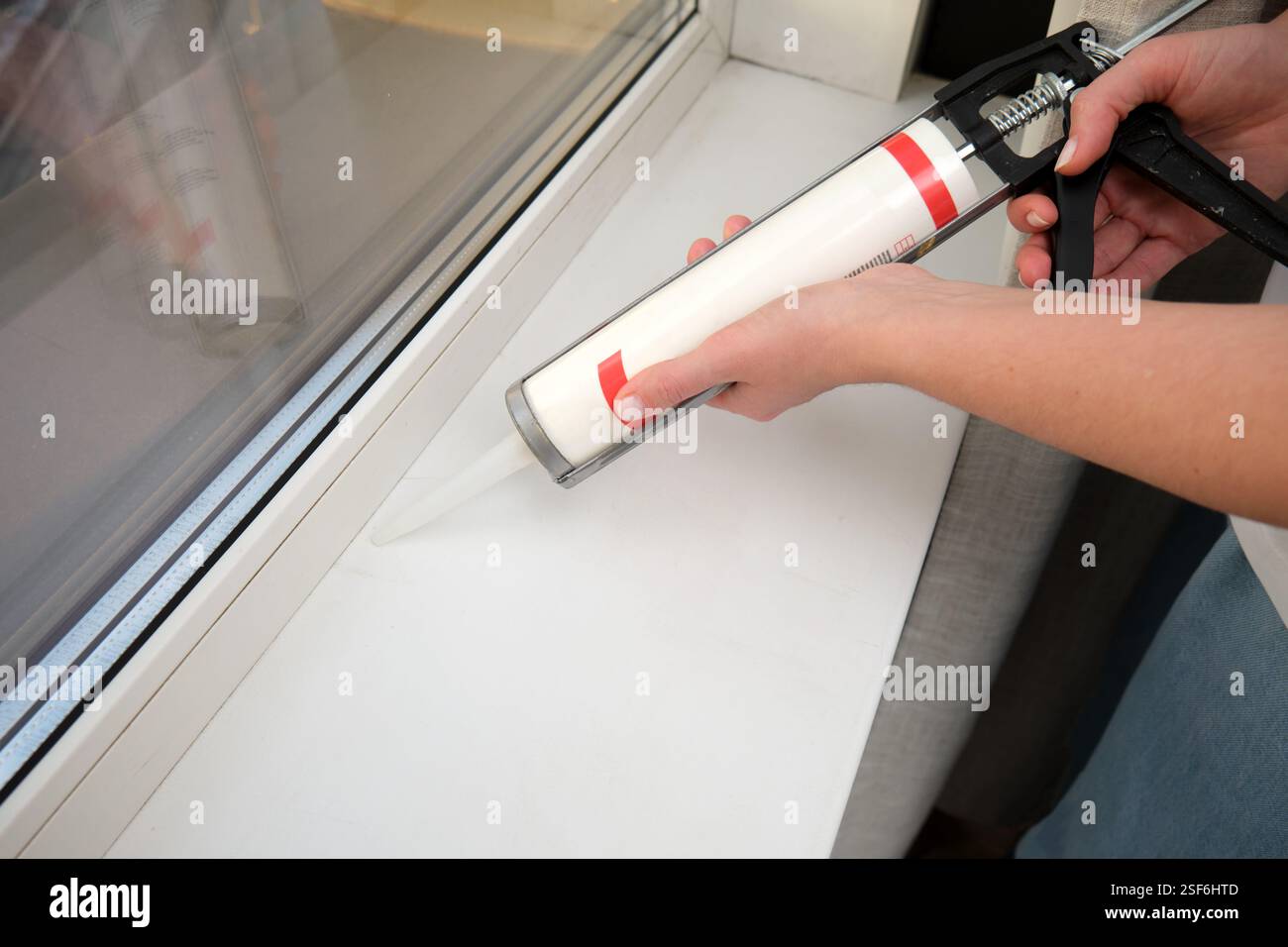 Hand applying sealant to window sill using caulking gun. Home renovation and window maintenance ...