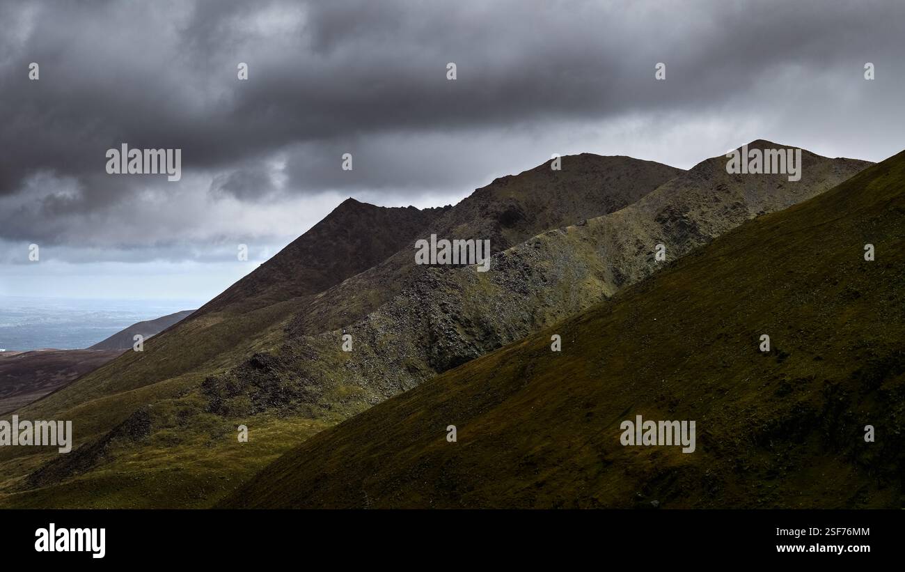 Jagged mountain ridges under a dramatic, cloudy sky, visible lower ...
