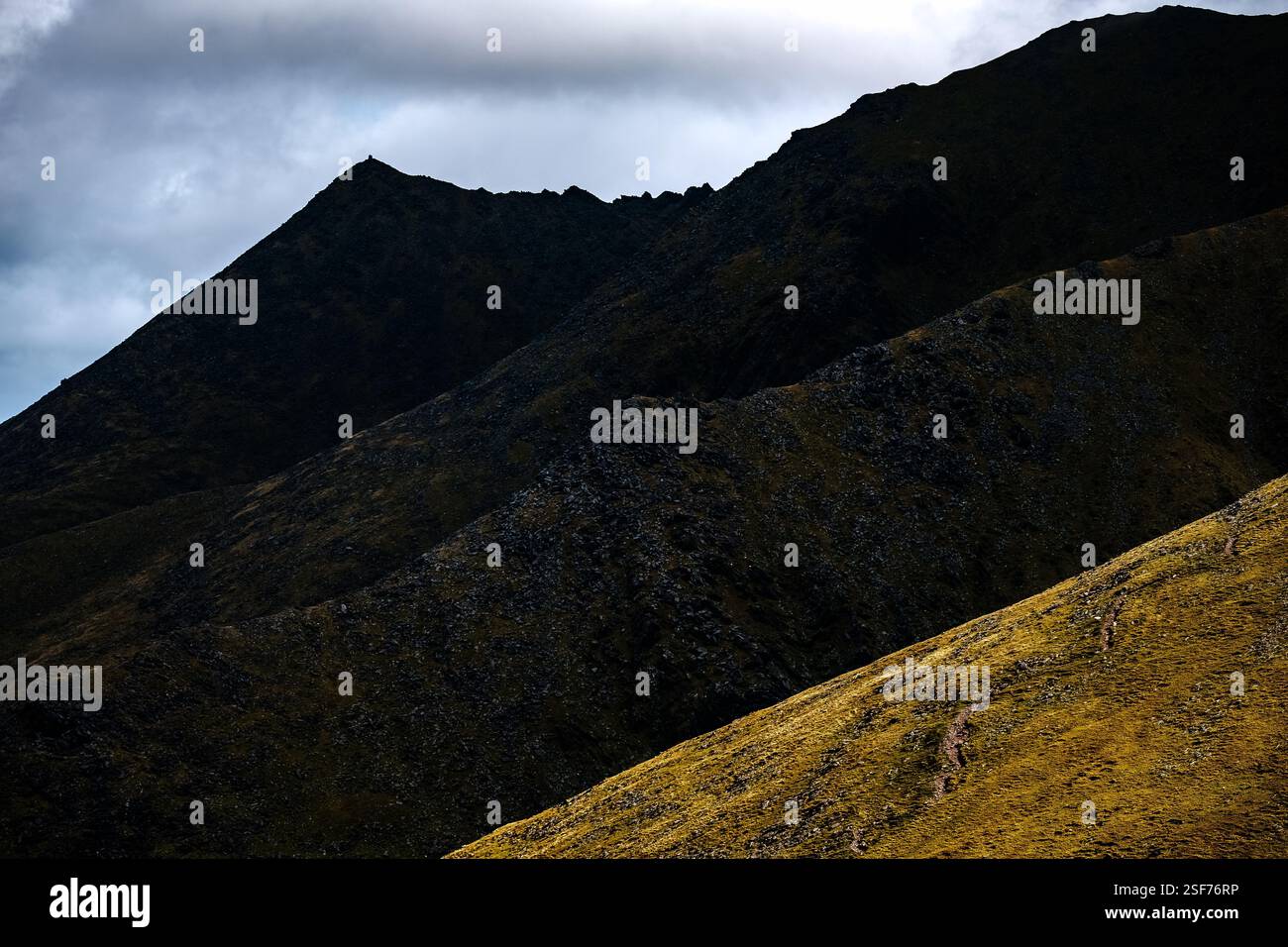 Multiple dark mountain summits, layered and steep, with a stormy sky ...