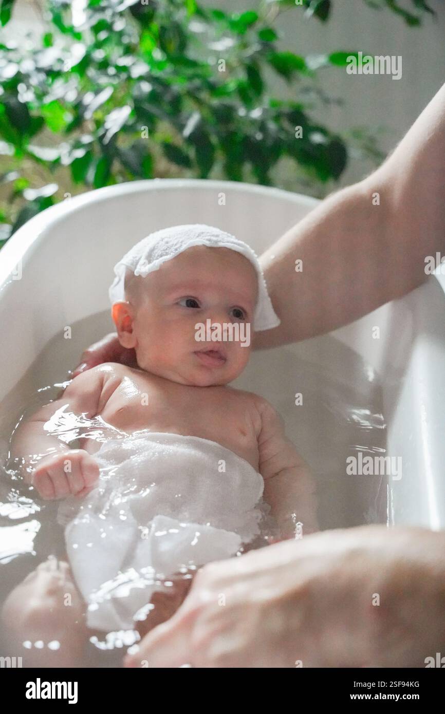 Bathing a 2-month-old baby in a small bath during the day. High quality ...