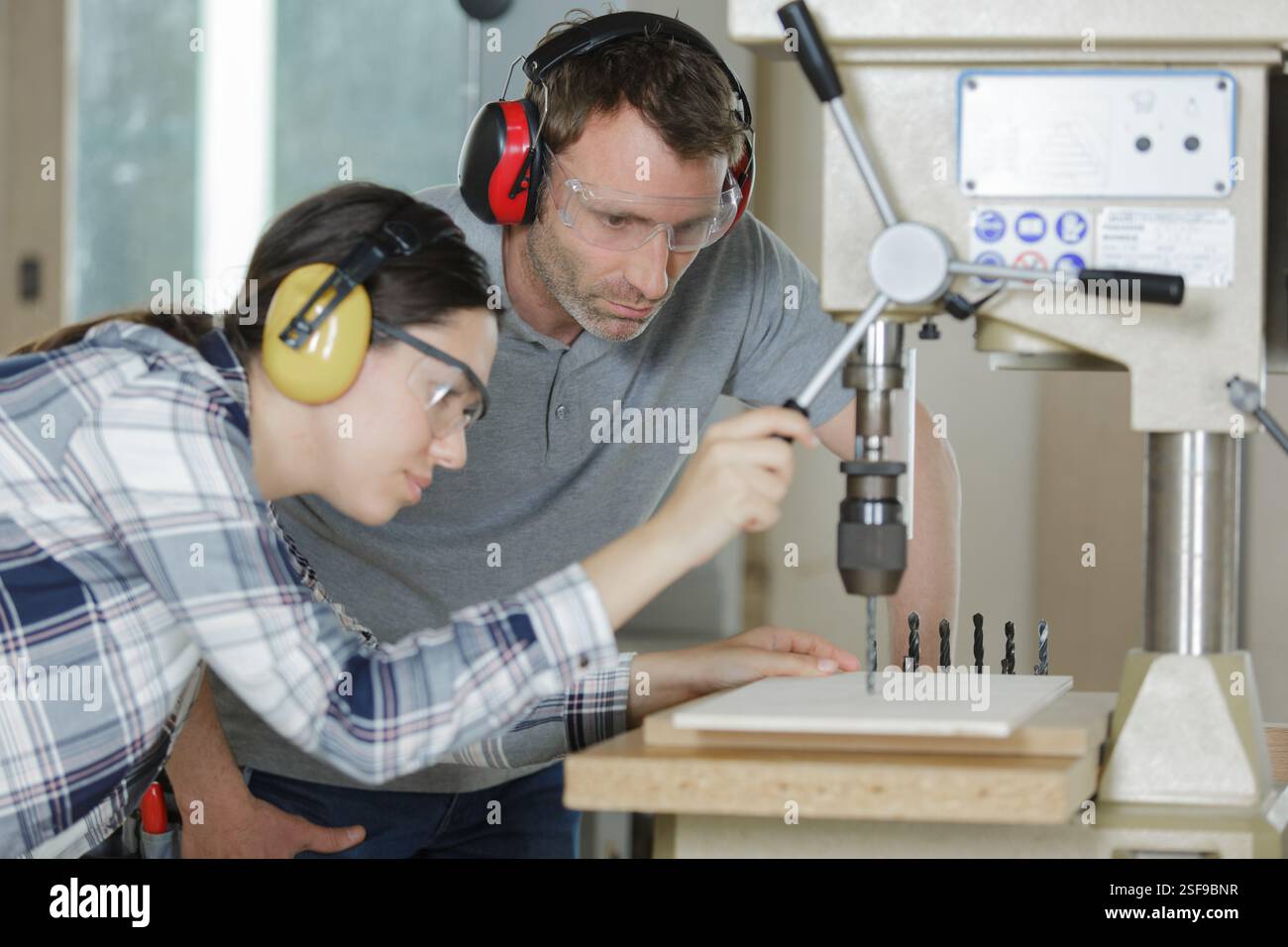 female apprentice using bench drill under supervision Stock Photo - Alamy