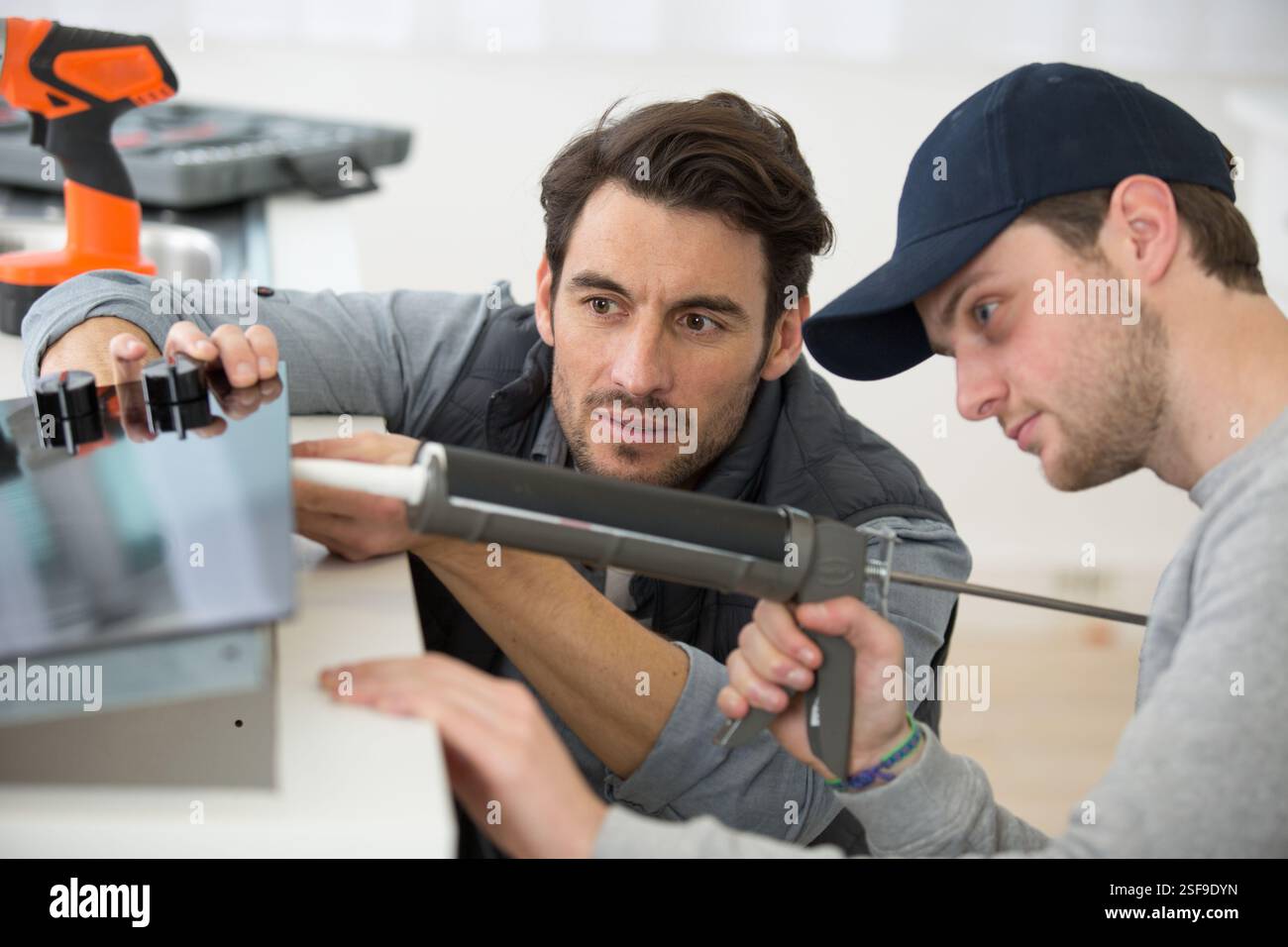 apprentice being advised how to apply caulk to window Stock Photo - Alamy