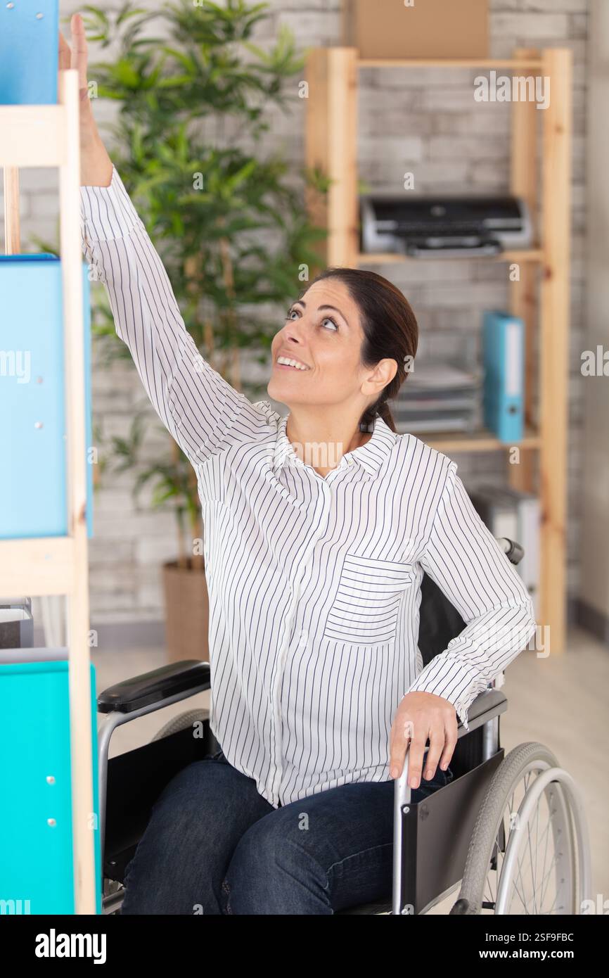 woman in wheelchair reaching for book from high shelf Stock Photo - Alamy