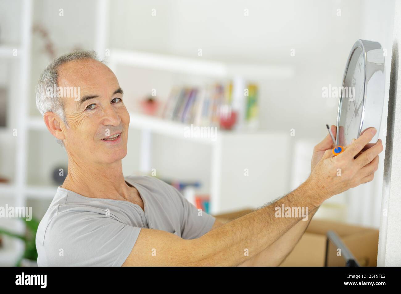 serious elderly man in casual outfit holding wall clock Stock Photo - Alamy