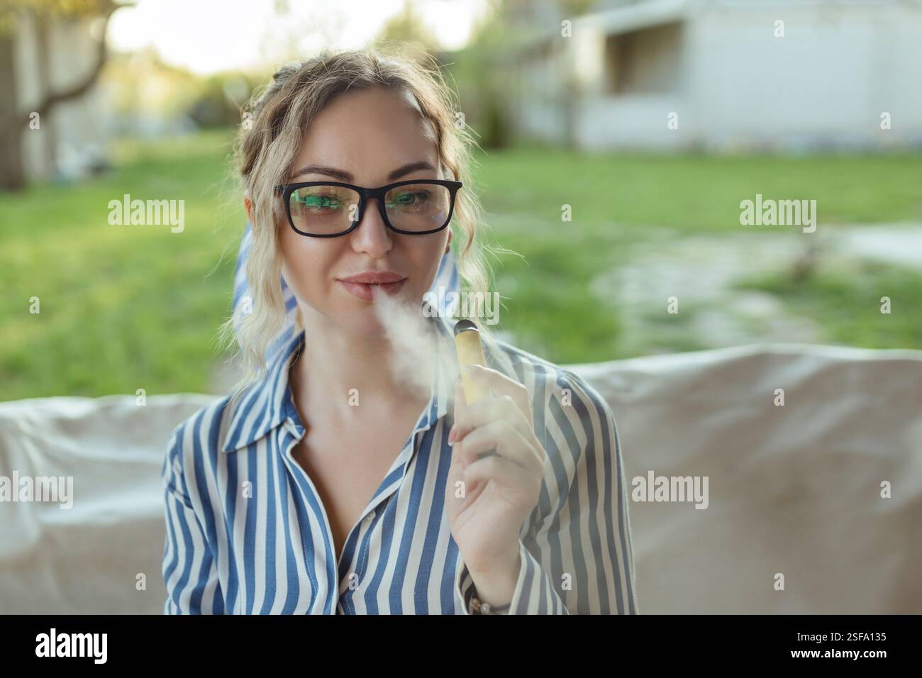 Beautiful woman smoking e-cigarette on the street and use smartphone ...