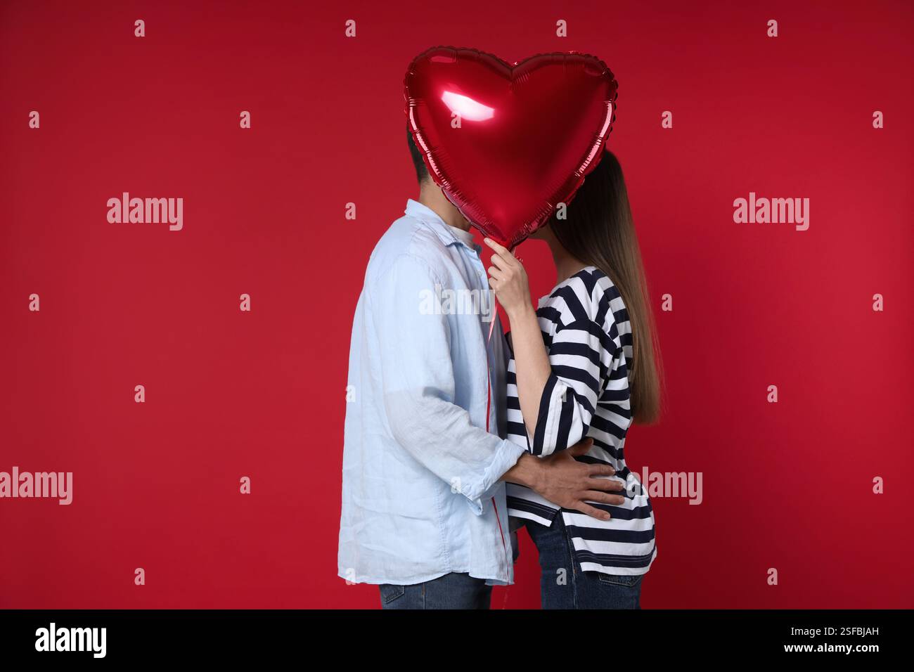 Lovely couple kissing behind heart shaped balloon on red background ...