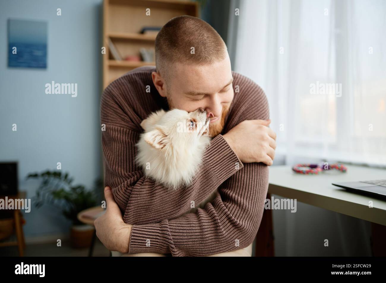 Man hugging fluffy white dog in comfortable home setting with bookshelf ...
