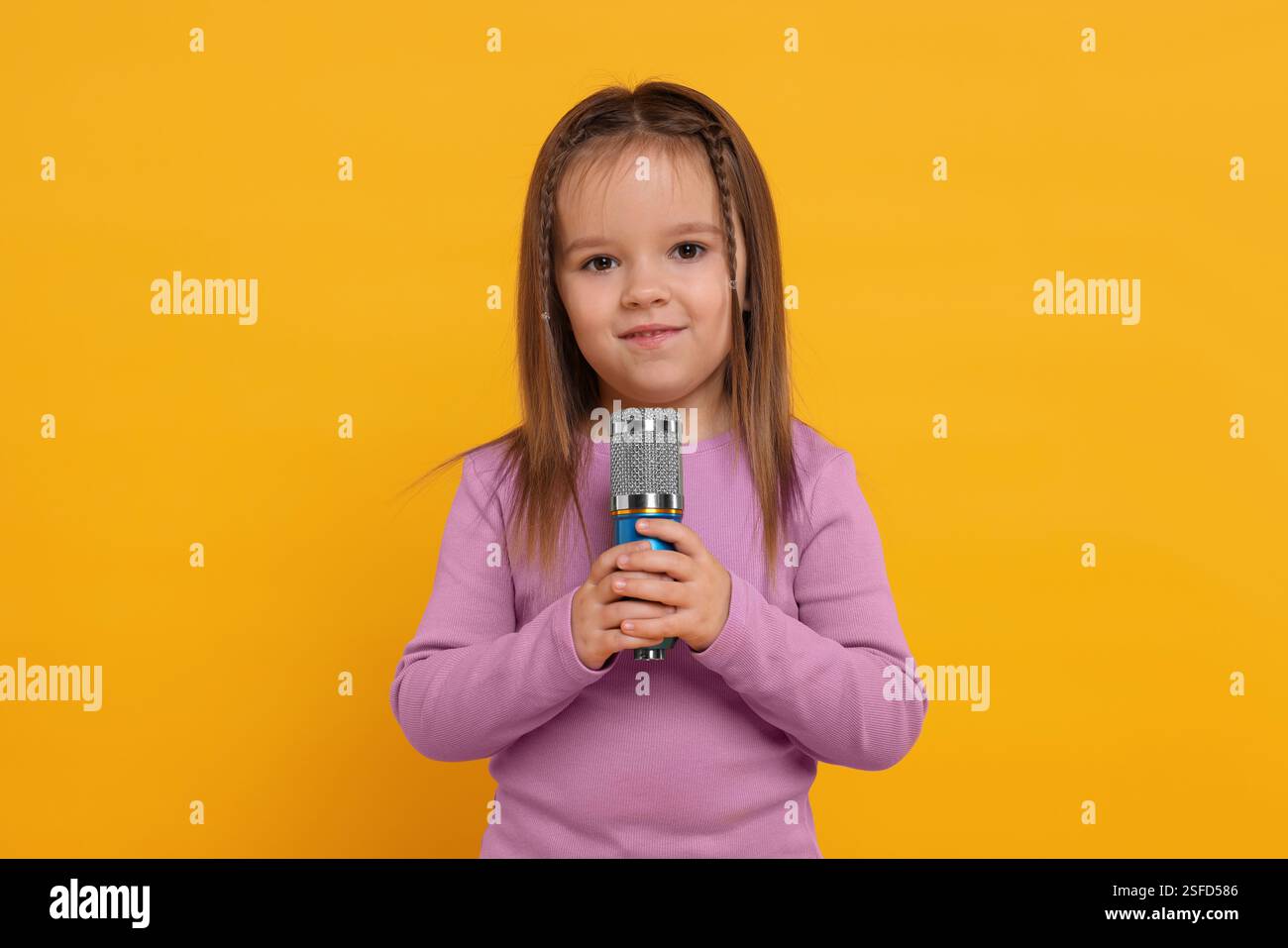Cute girl with microphone on orange background Stock Photo - Alamy