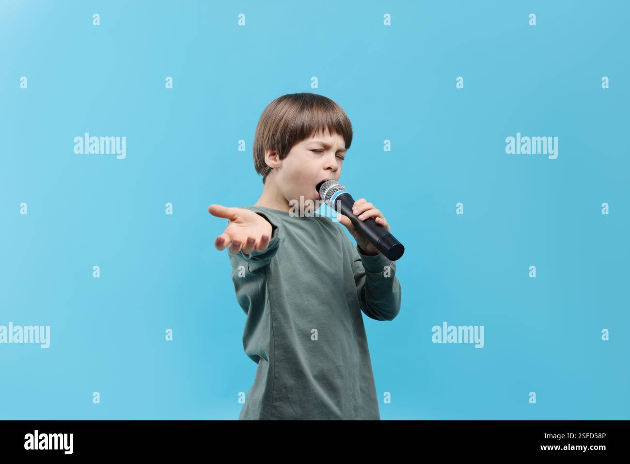 Cute boy with microphone singing on light blue background Stock Photo ...