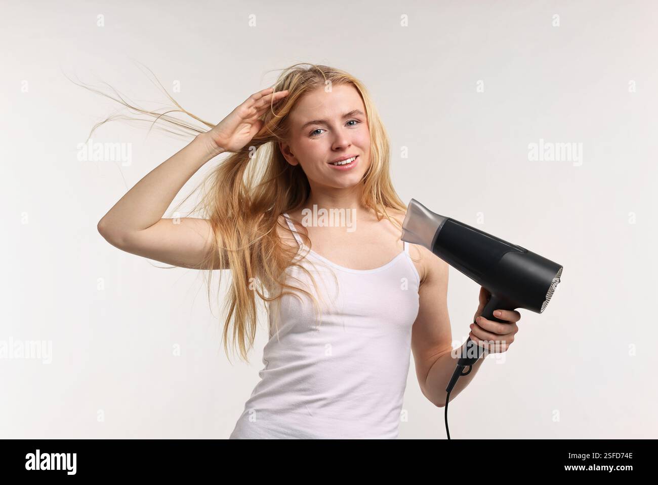 Beautiful young woman drying her hair with hairdryer on light grey ...