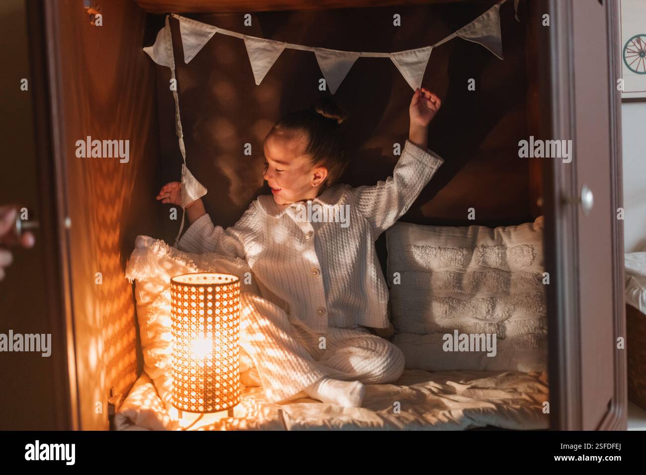 Smiling girl in leisurewear sitting in a cupboard den decorated with ...