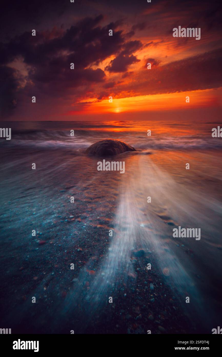Receding sea washing past a rock on a sandy beach at sunset, Lithuania ...
