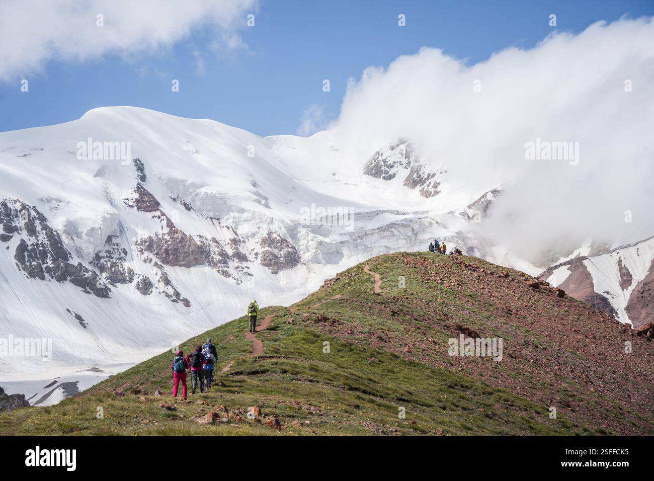 Group of hikers enjoying ridgeline views under snowy peak and glacier ...