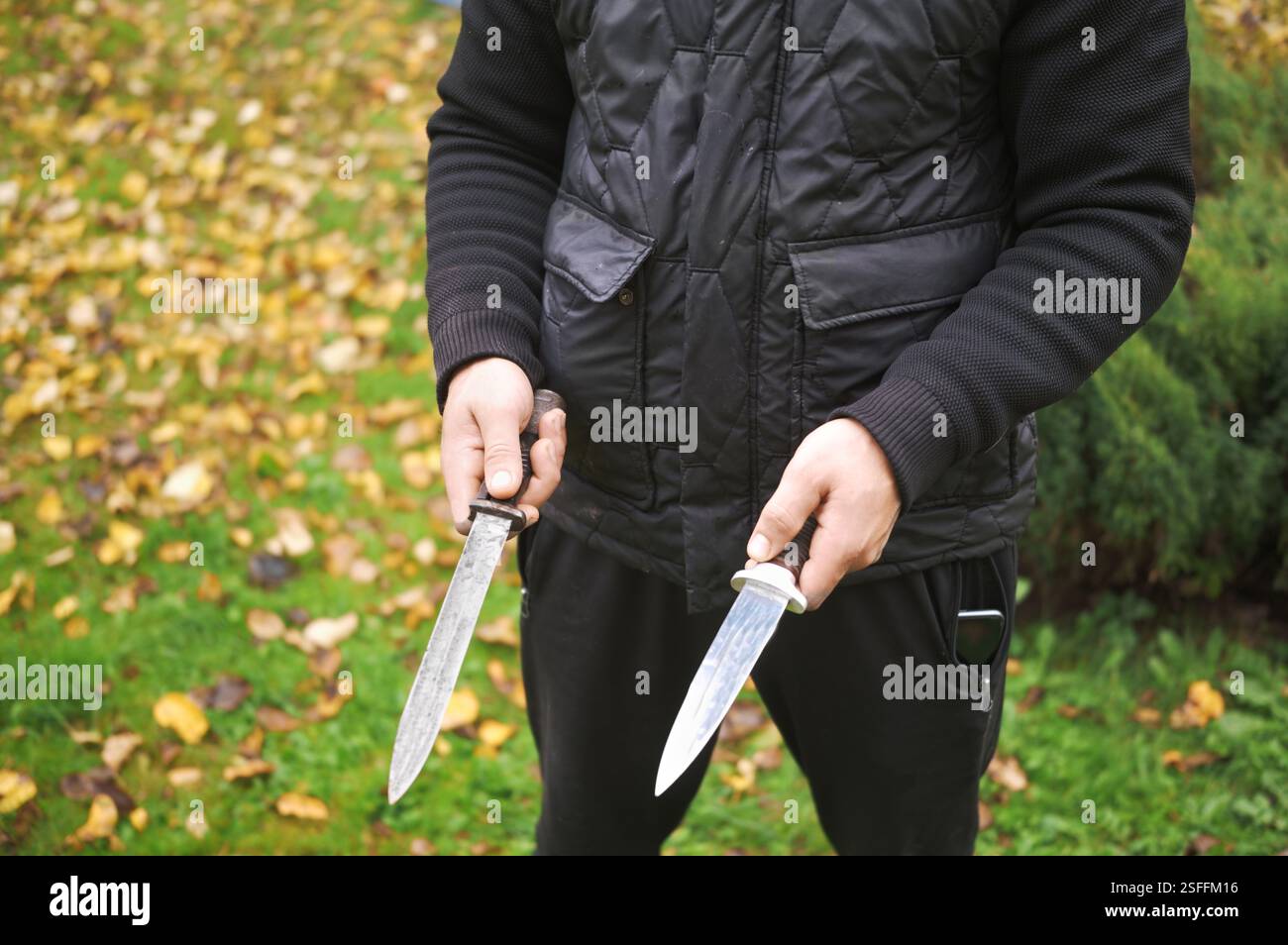 a man holding two knives in front of himself, outdoor shot Stock Photo ...