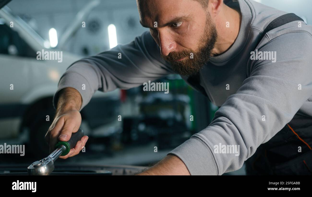 Caucasian mechanic in uniform repairing engine fixing motor inside open ...