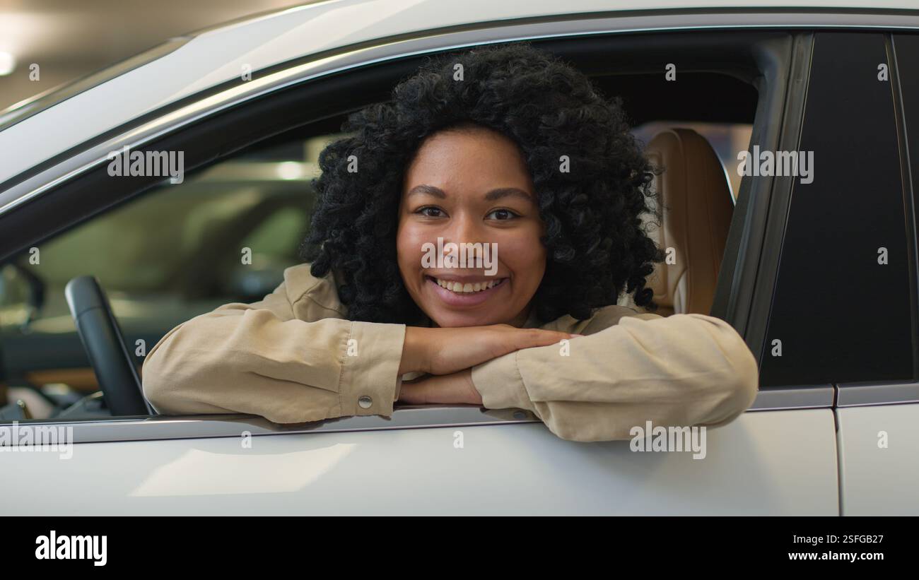 Happy smiling African American ethnic woman driver inside new car salon ...