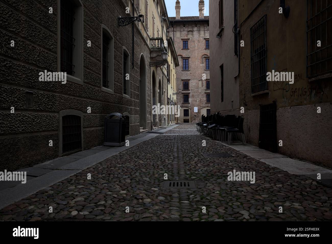 Narrow alley paved with cobblestone in the shade that leads to a square ...