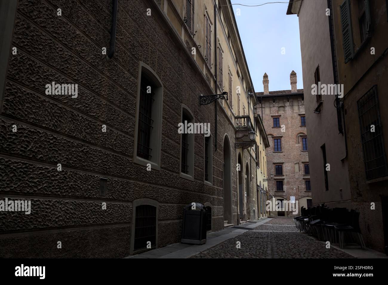 Narrow alley paved with cobblestone in the shade that leads to a square ...