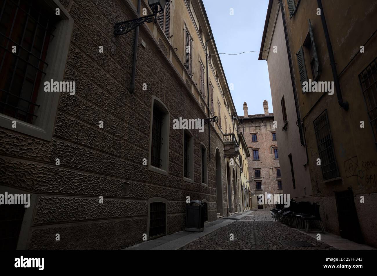 Narrow alley paved with cobblestone in the shade that leads to a square ...
