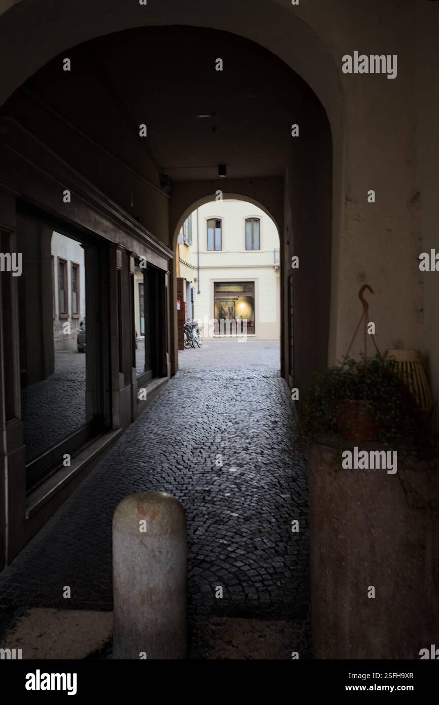 Cobbled archway in the shade under a building that leads to a square in ...