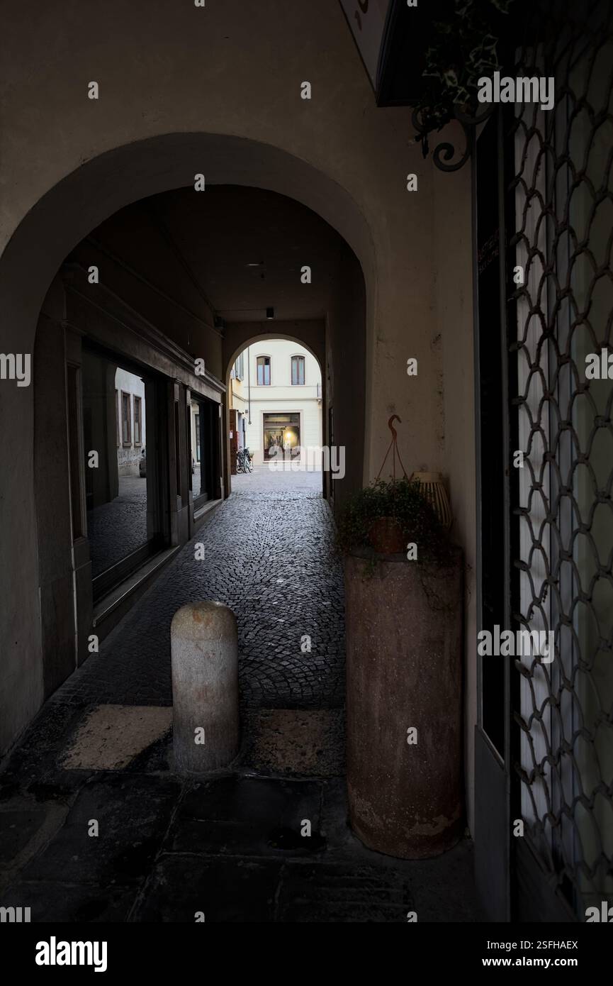 Cobbled archway in the shade under a building that leads to a square in ...